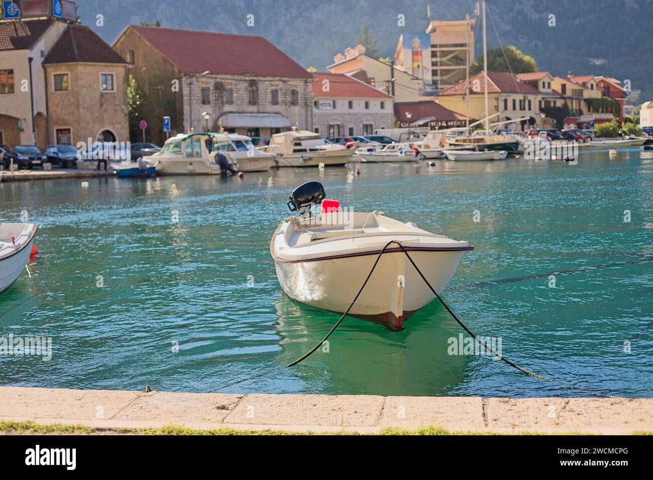 A solitary white boat floats on the calm waters of Kotor Bay, the ...