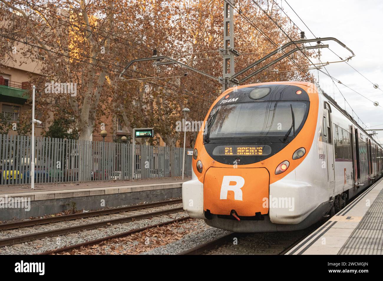 An orange train arrives at the station and is stationary on the tracks ...