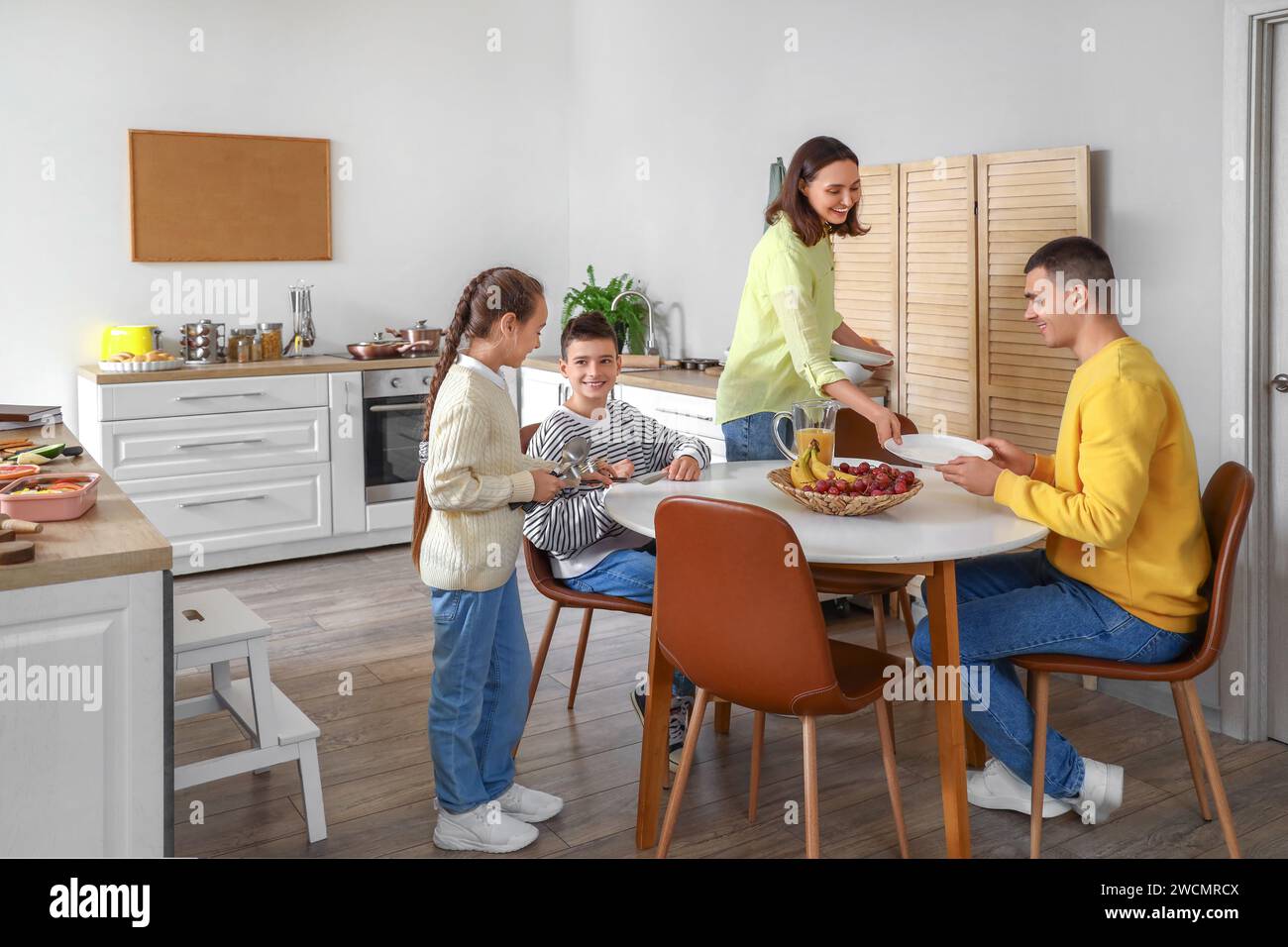 Happy family setting dining table in kitchen Stock Photo - Alamy