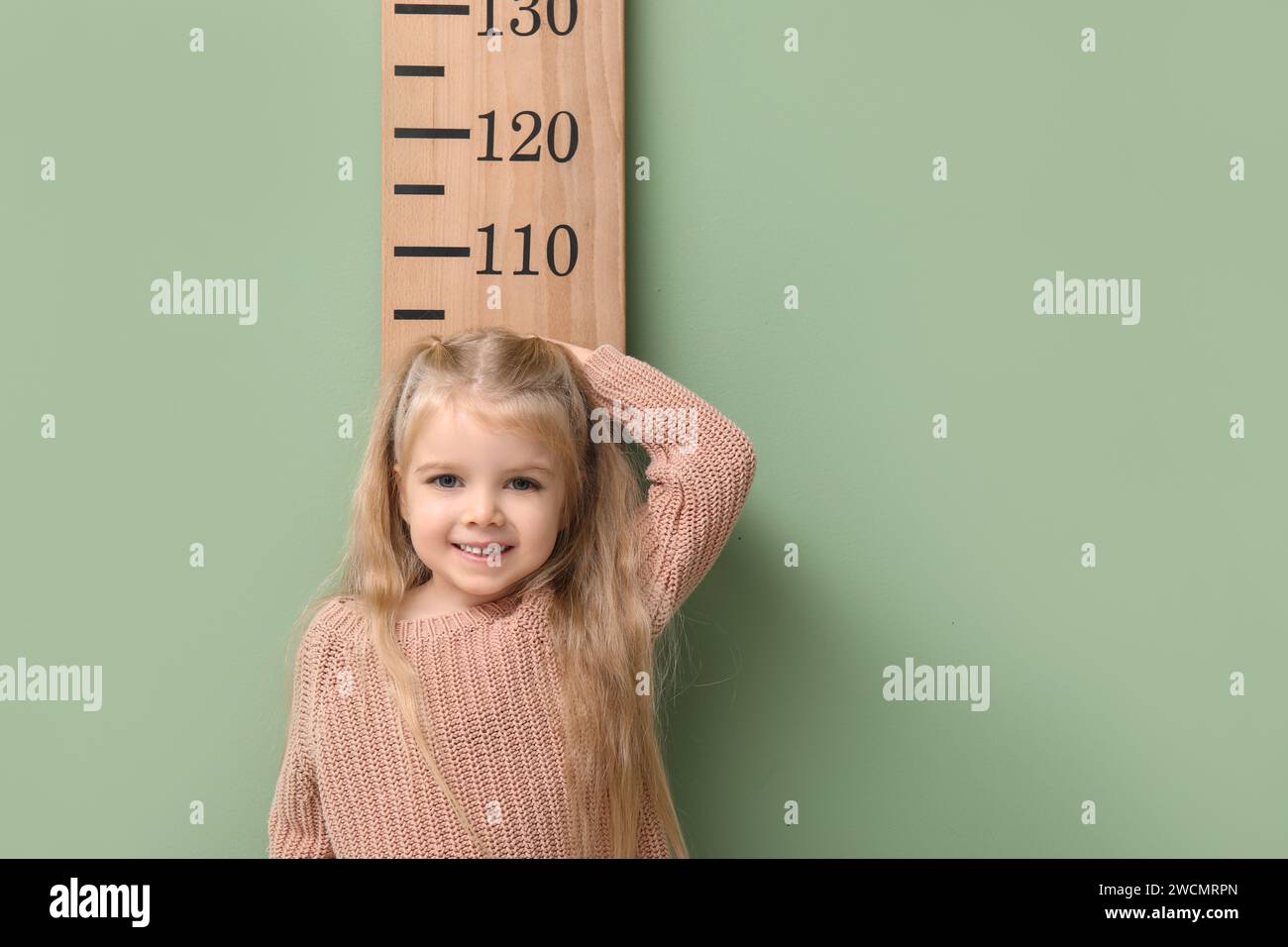 Cute little girl measuring height on green background Stock Photo - Alamy