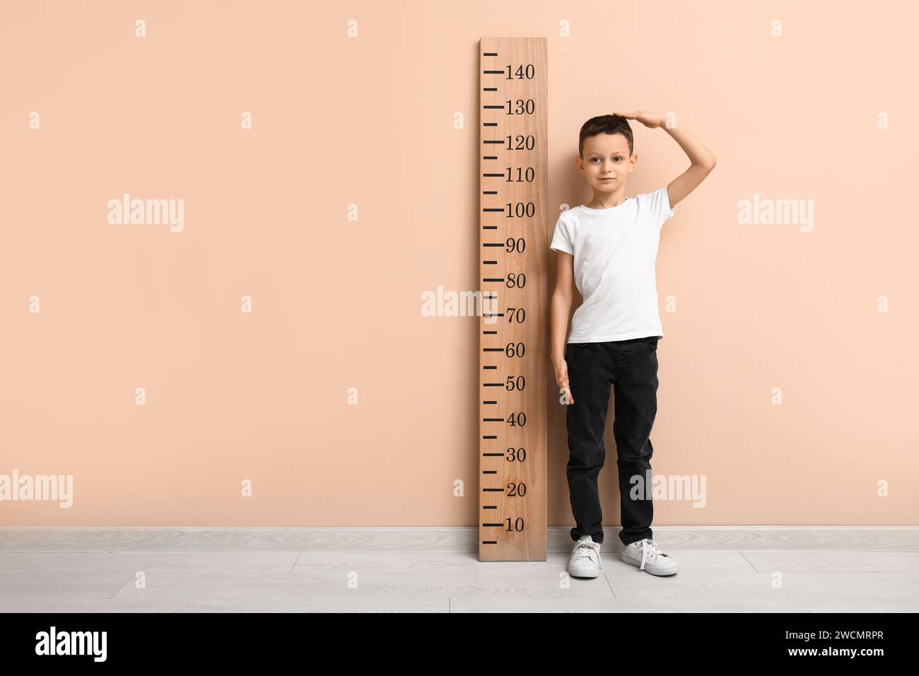 Cute little boy measuring height near beige wall Stock Photo - Alamy