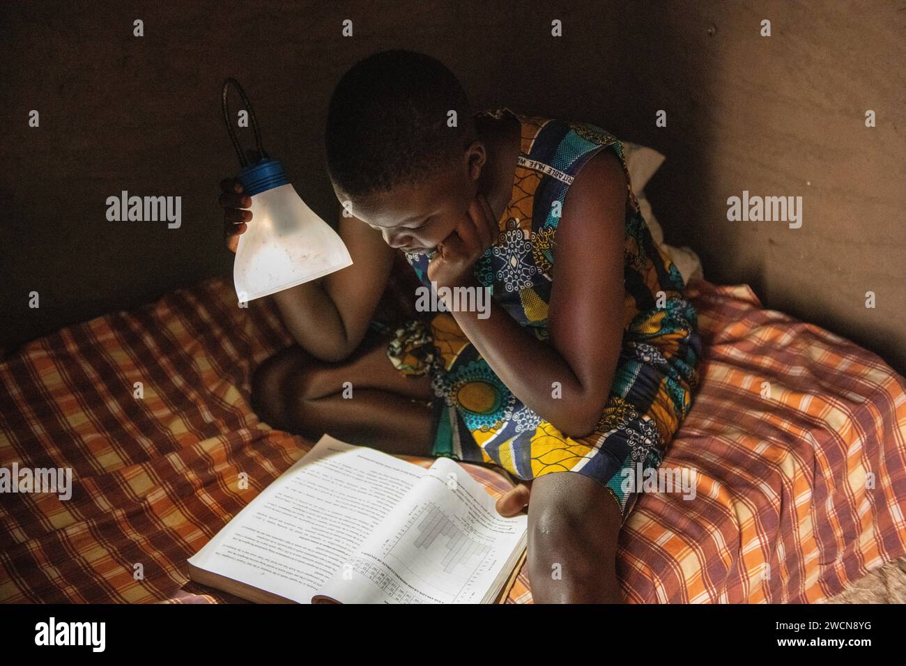 Uganda, Adjumani. A child studies by the light from a solar powered ...