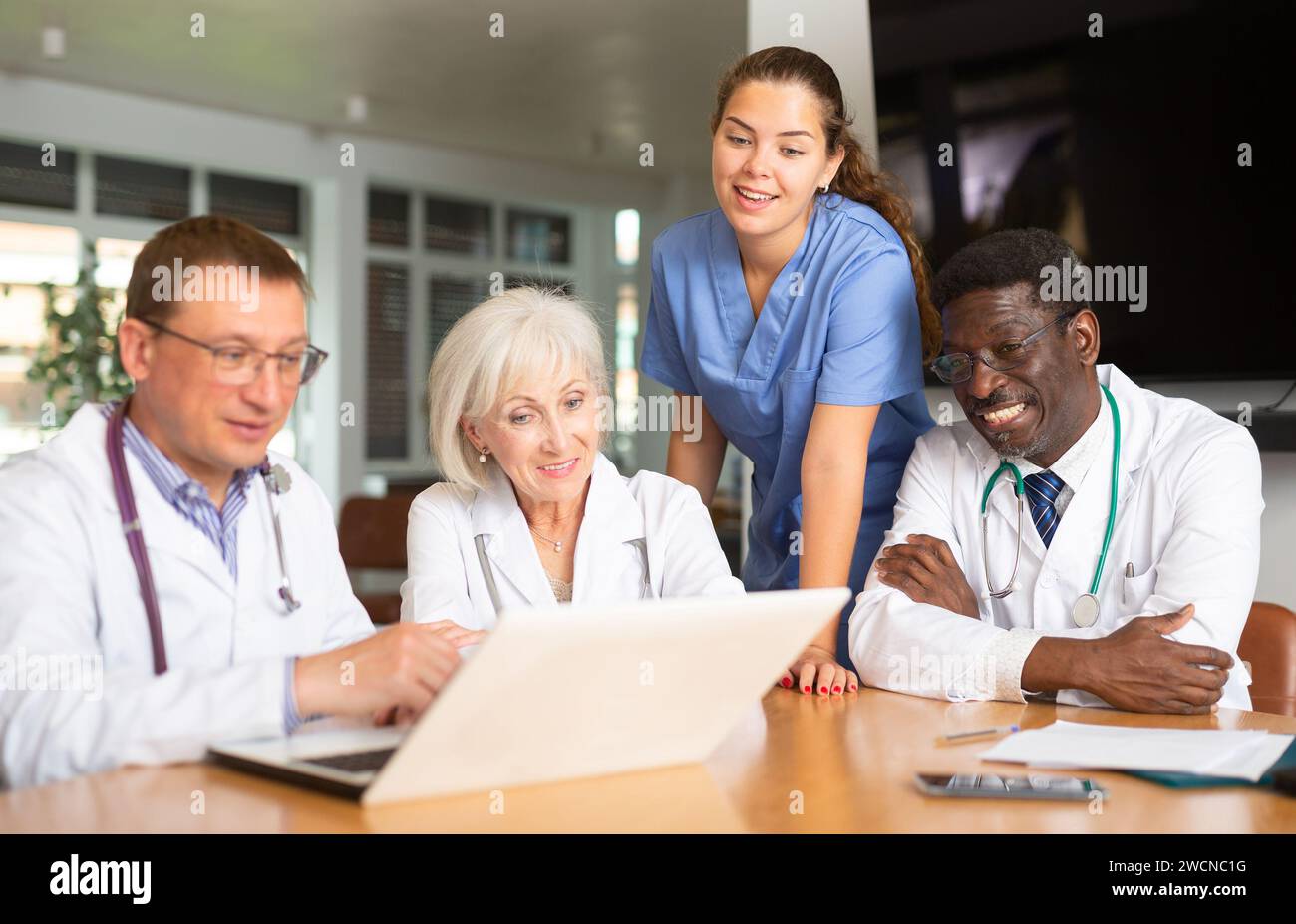 Doctors sitting around the table looking at the notebook Stock Photo ...