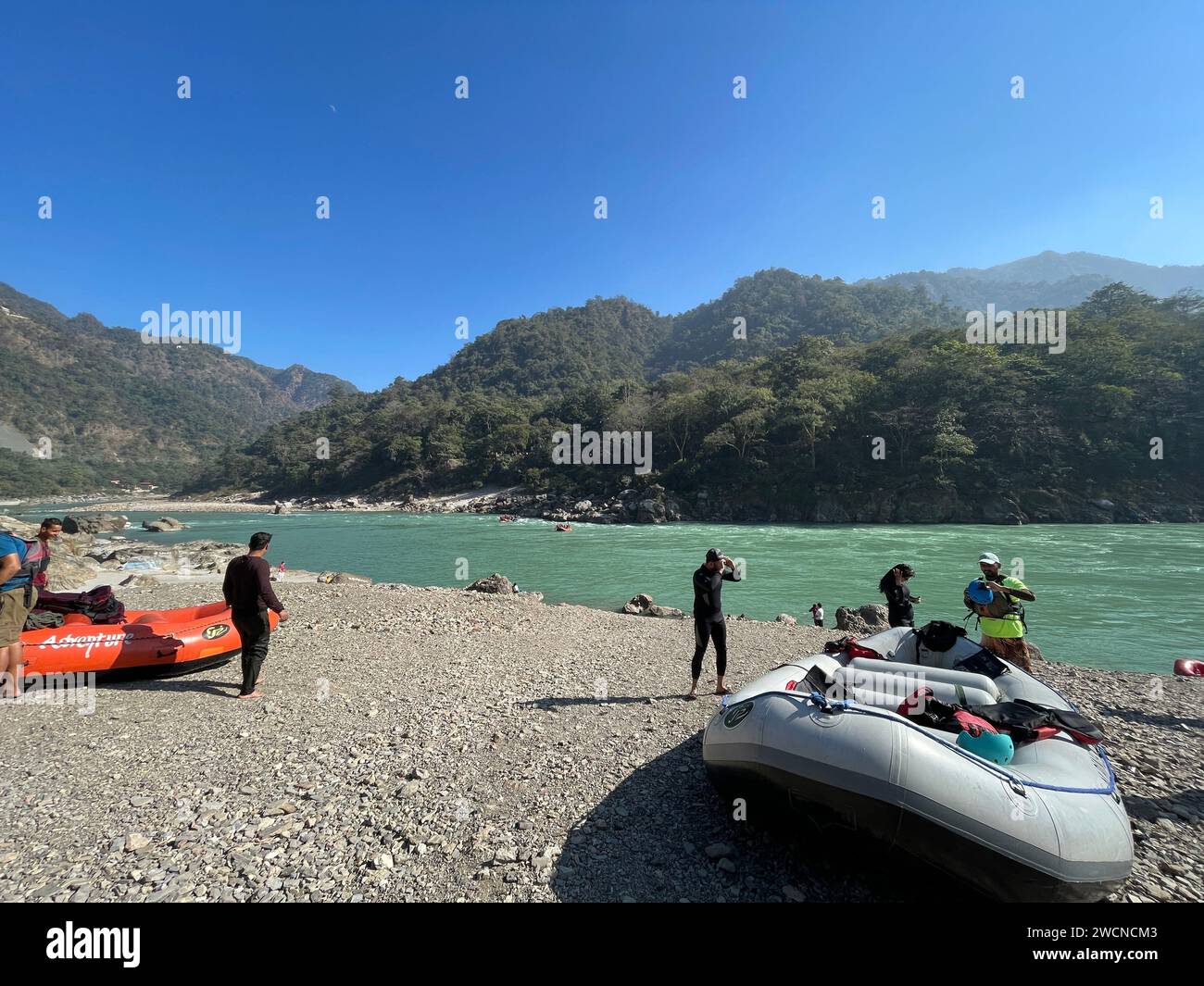 A group of people standing by a river with mountains in the background ...