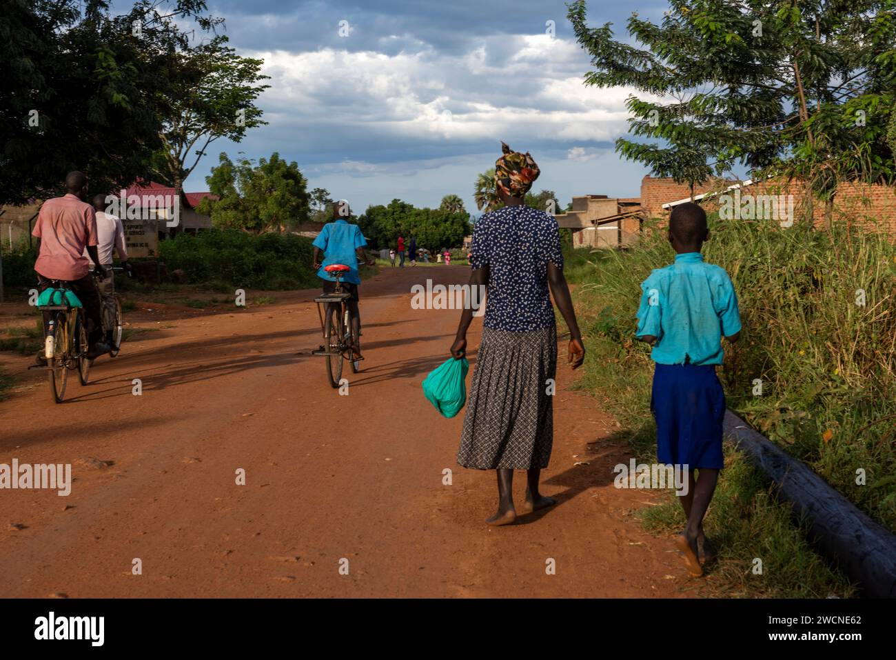 Uganda, Kitgum District. A boy walks home with his mother on the dirt ...
