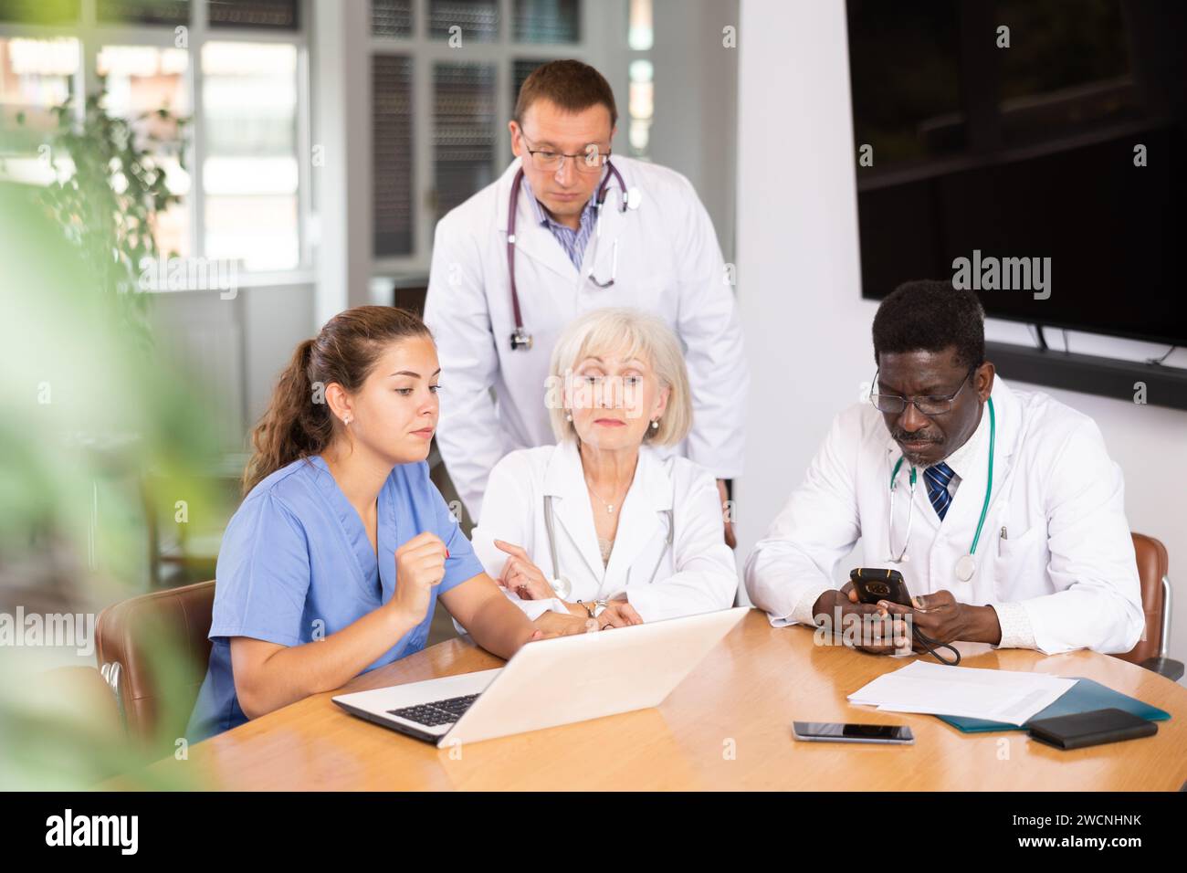Doctors sitting around the table looking at the notebook Stock Photo ...
