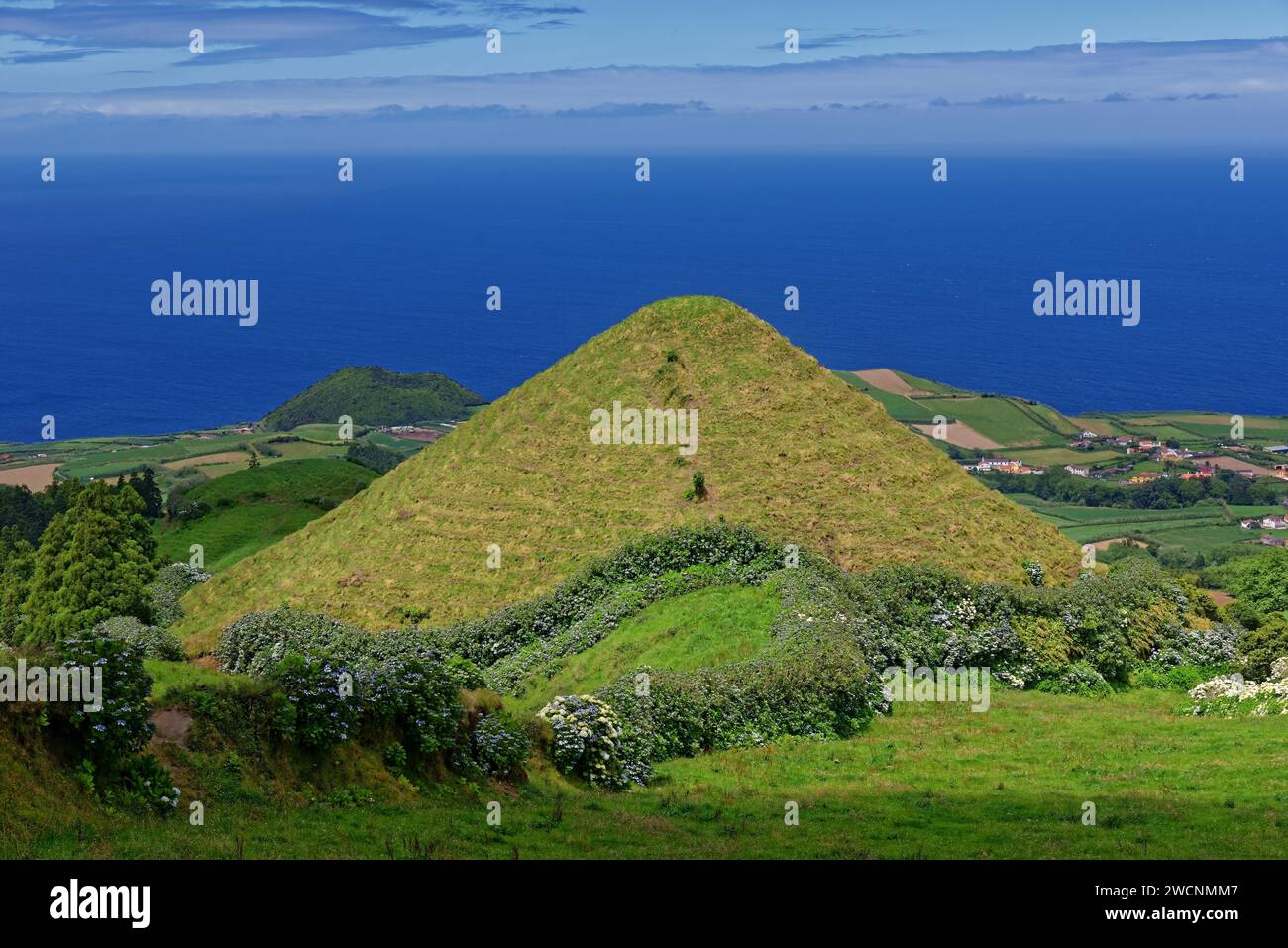 An isolated, green volcanic hill stands out, surrounded by agriculture ...
