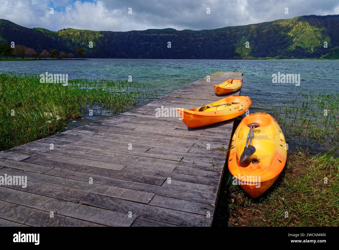 Three orange kayaks on the wooden jetty of the crater lake Lagoa Azul ...