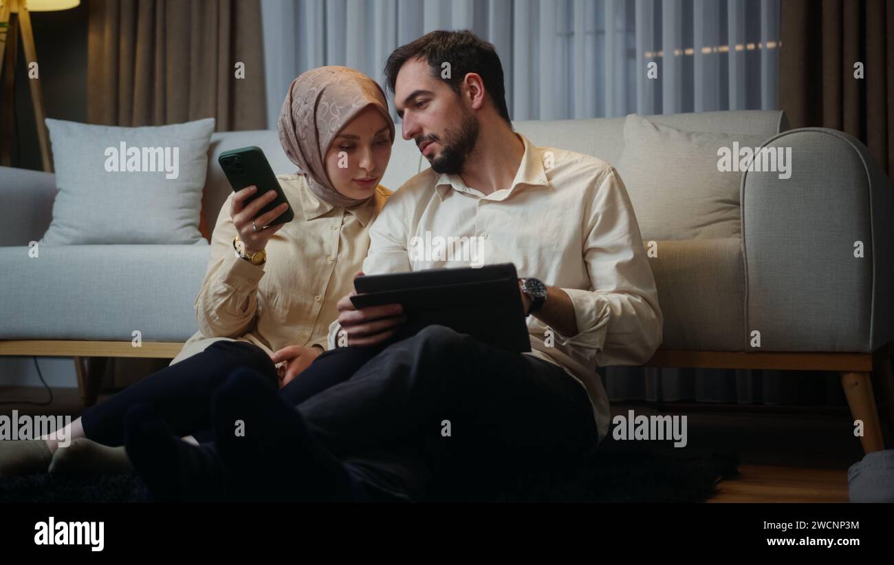 Young married couple leaning against the sofa sitting on floor, woman ...