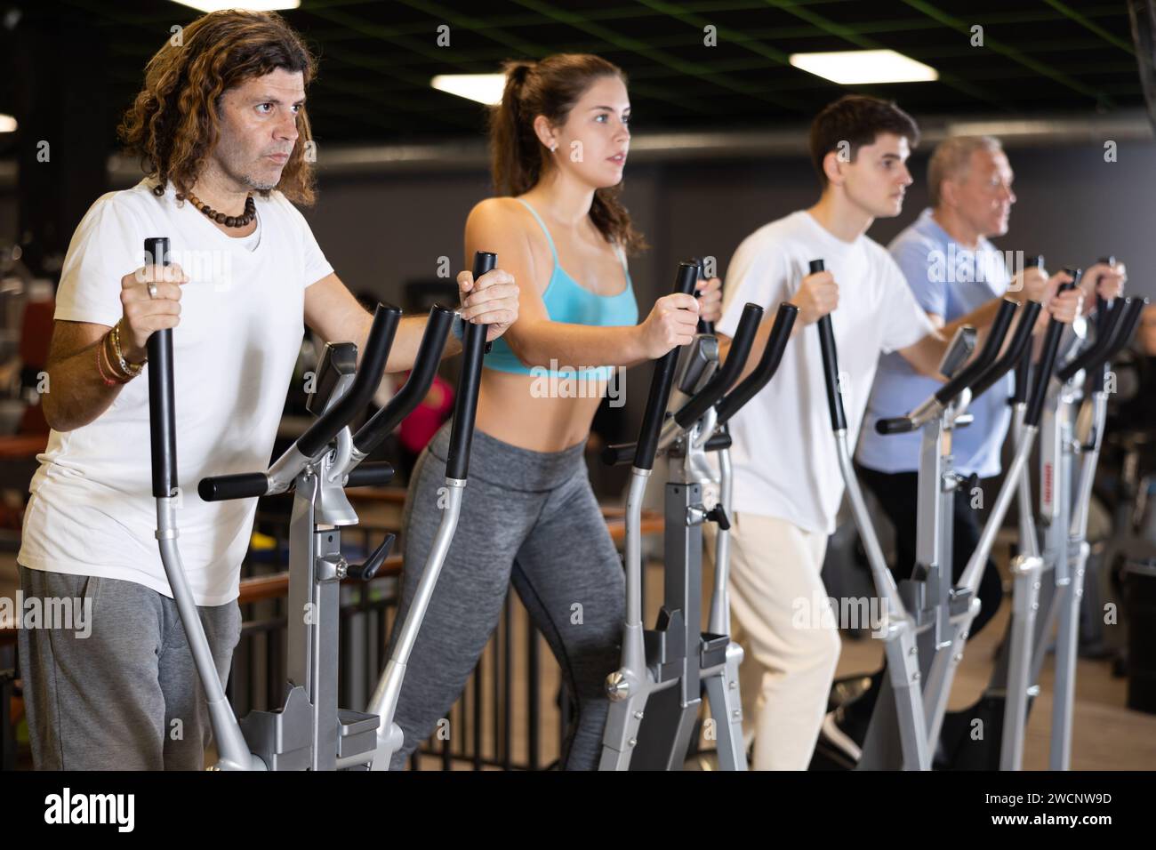Group of people of different ages train on elliptical trainers steppers ...