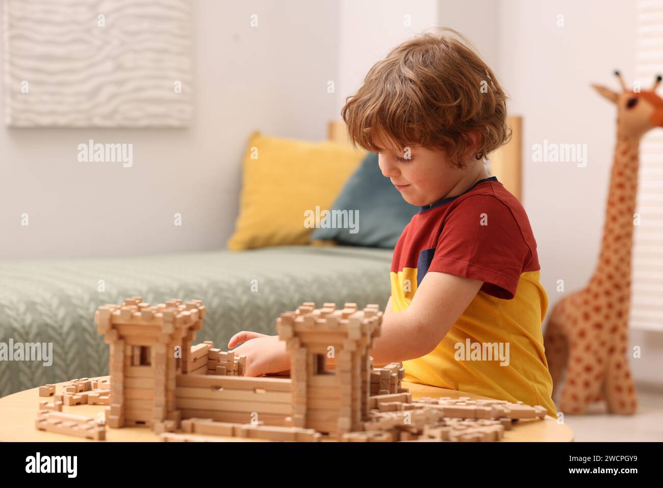Cute little boy playing with wooden construction set at table in room ...