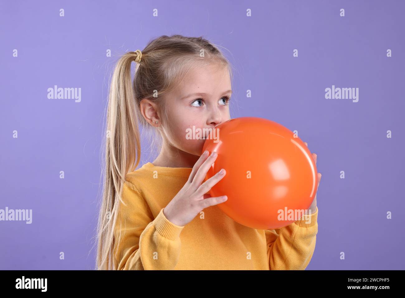 Cute little girl inflating orange balloon on violet background Stock ...