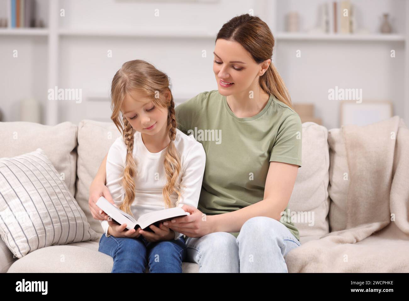 Girl and her godparent reading Bible together on sofa at home Stock ...