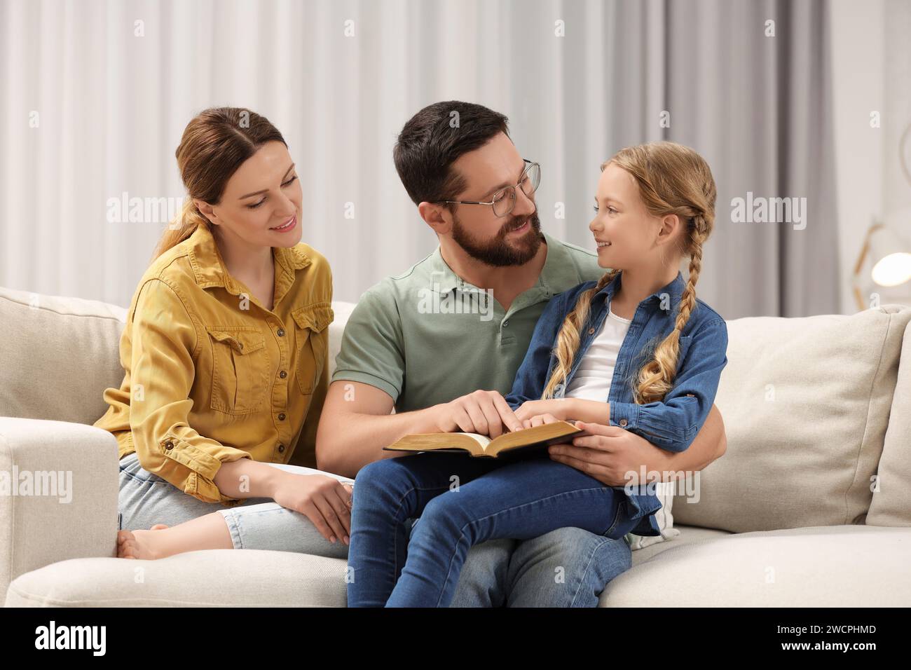 Girl and her godparents reading Bible together on sofa at home Stock ...