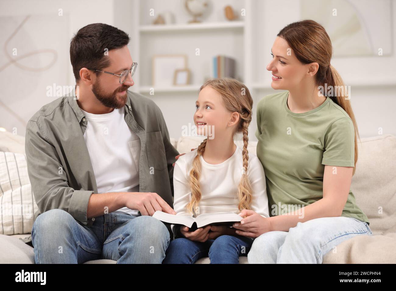 Girl and her godparents reading Bible together on sofa at home Stock ...