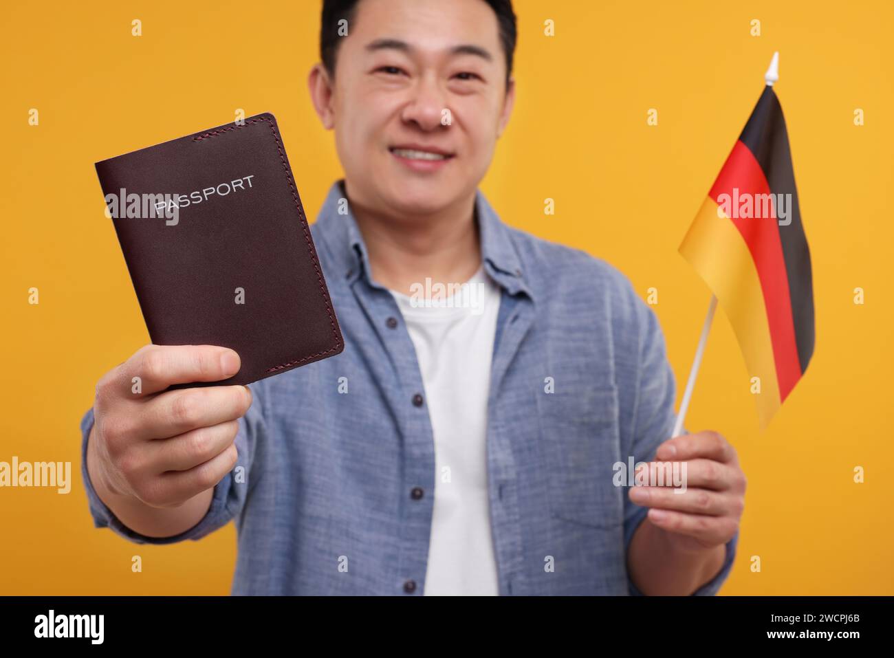 Immigration. Happy man with passport and flag of Germany on orange ...