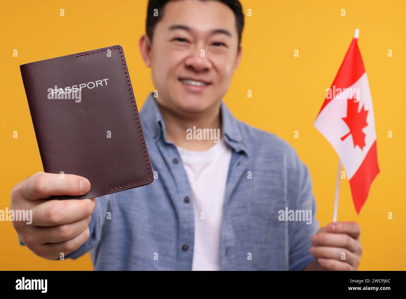 Immigration. Happy man with passport and flag of Canada on orange ...