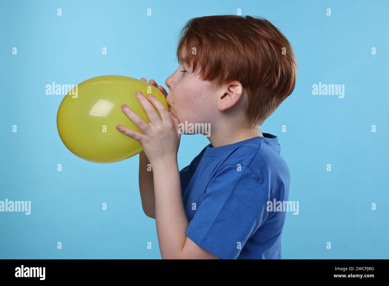 Boy inflating yellow balloon on light blue background Stock Photo - Alamy