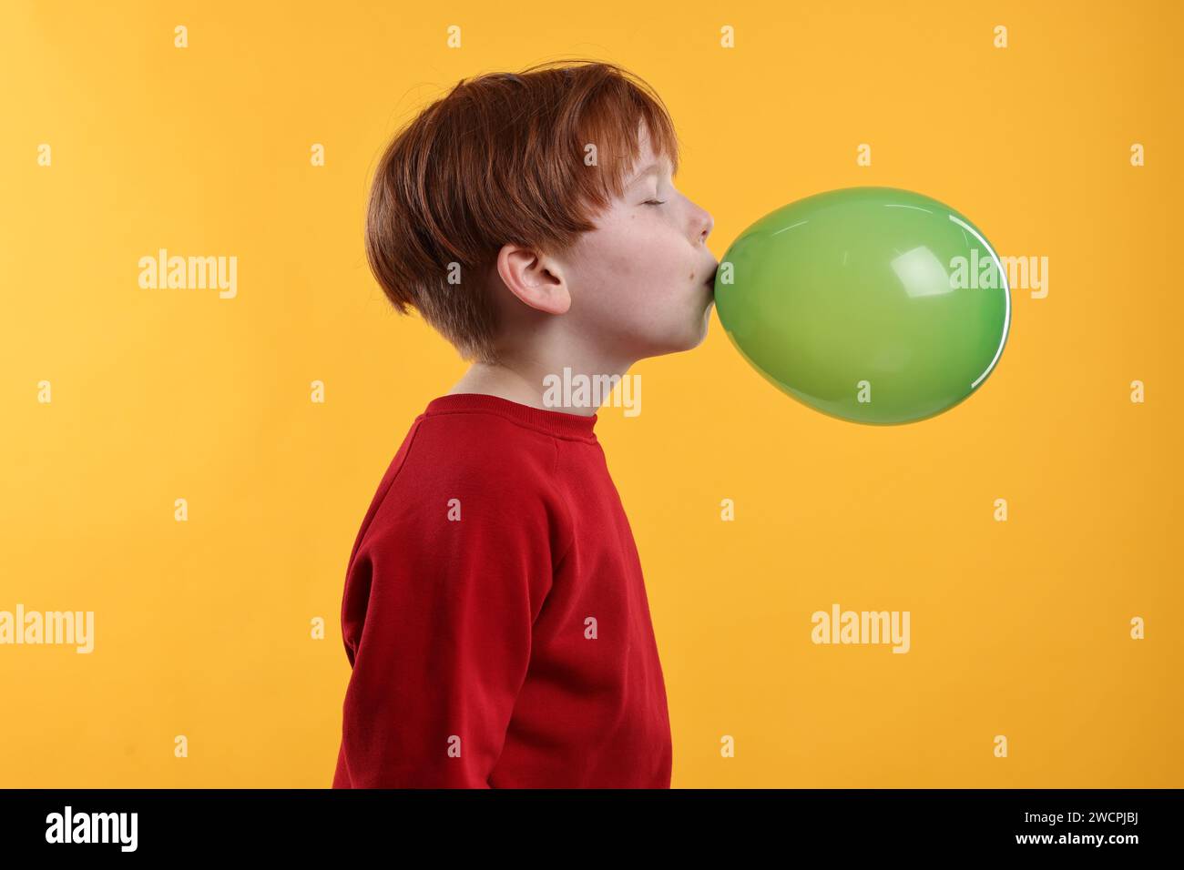 Boy inflating green balloon on orange background Stock Photo - Alamy