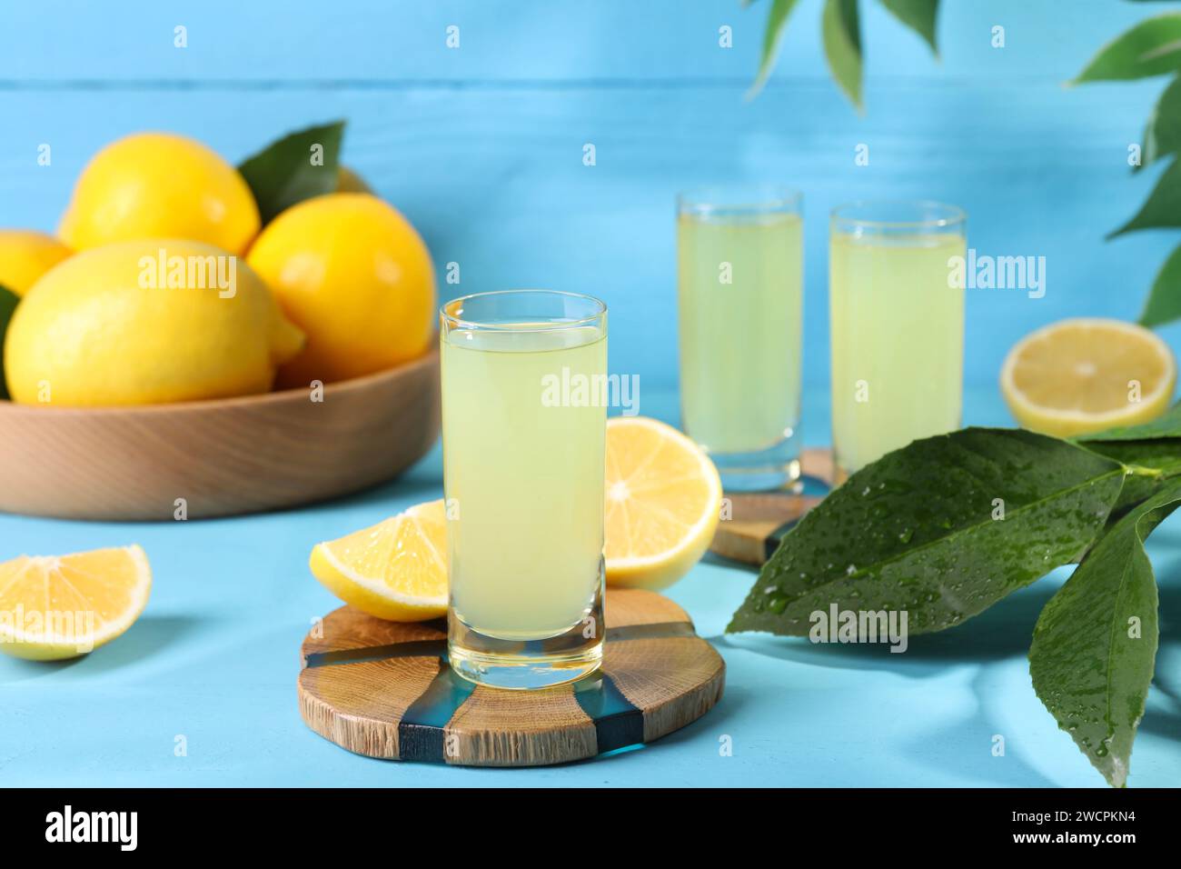 Tasty limoncello liqueur, lemons and green leaves on light blue table ...