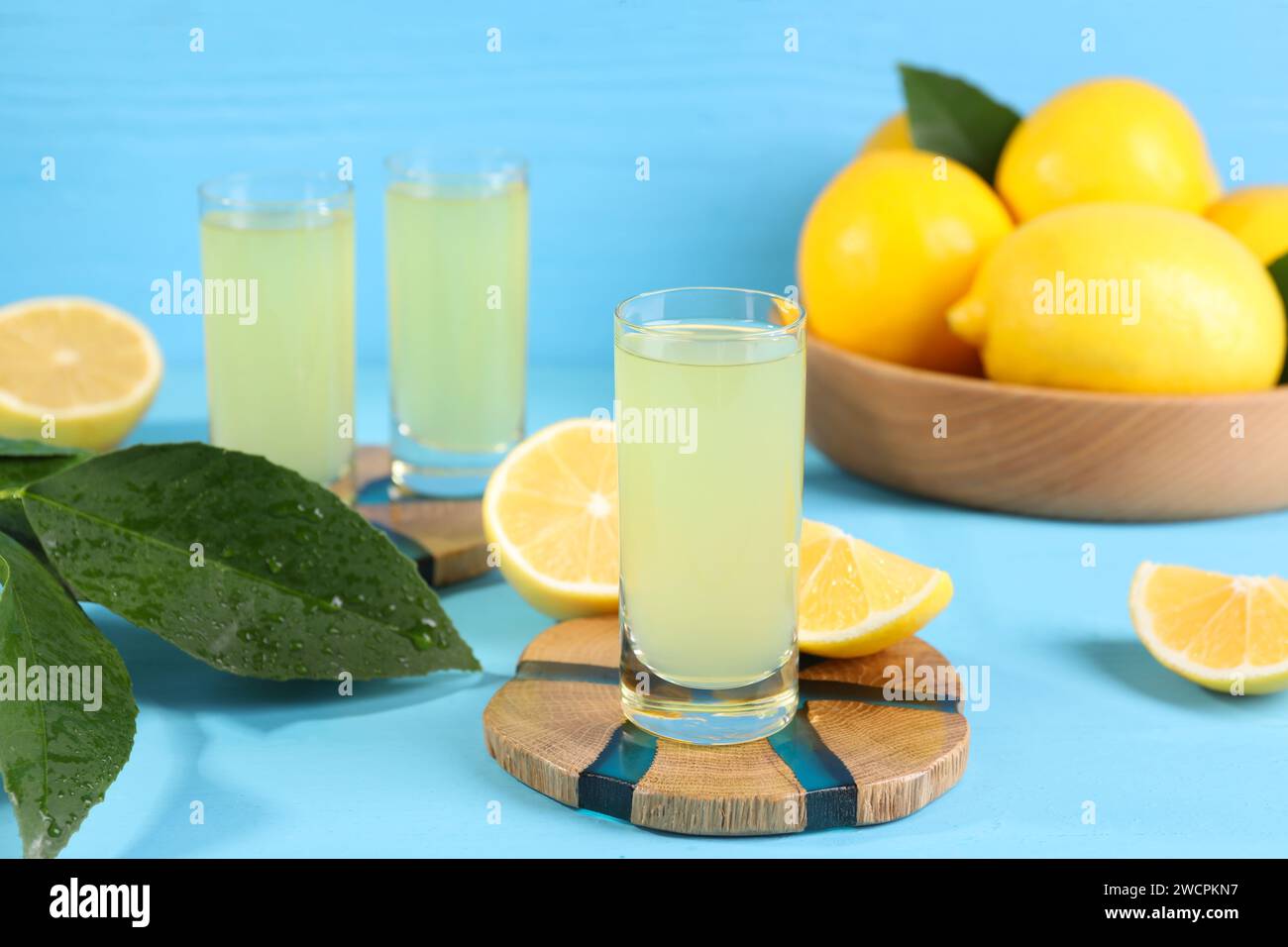 Tasty limoncello liqueur, lemons and green leaves on light blue table ...