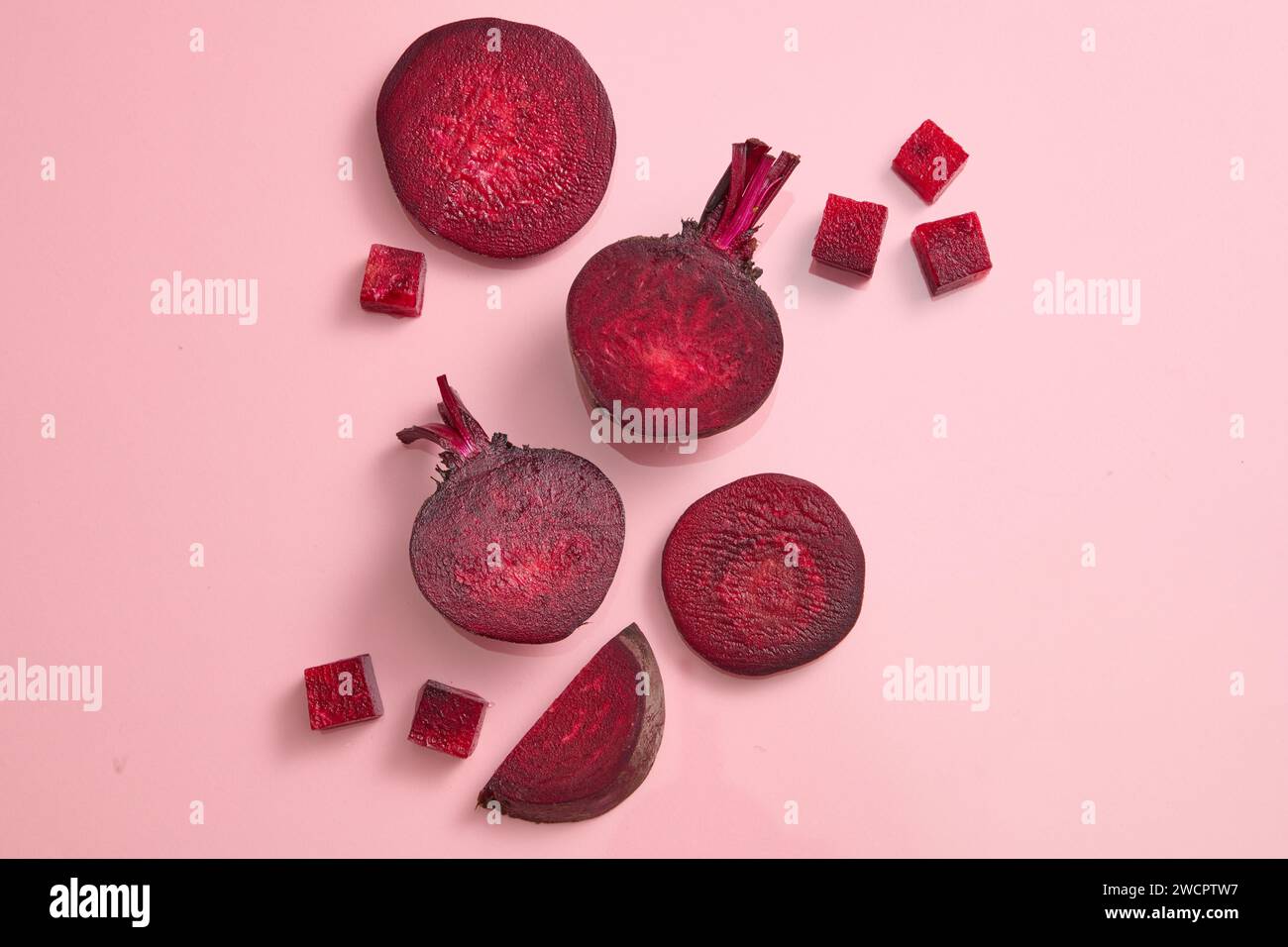 Beetroot cut in halves, slices and cubes are decorated against pink ...