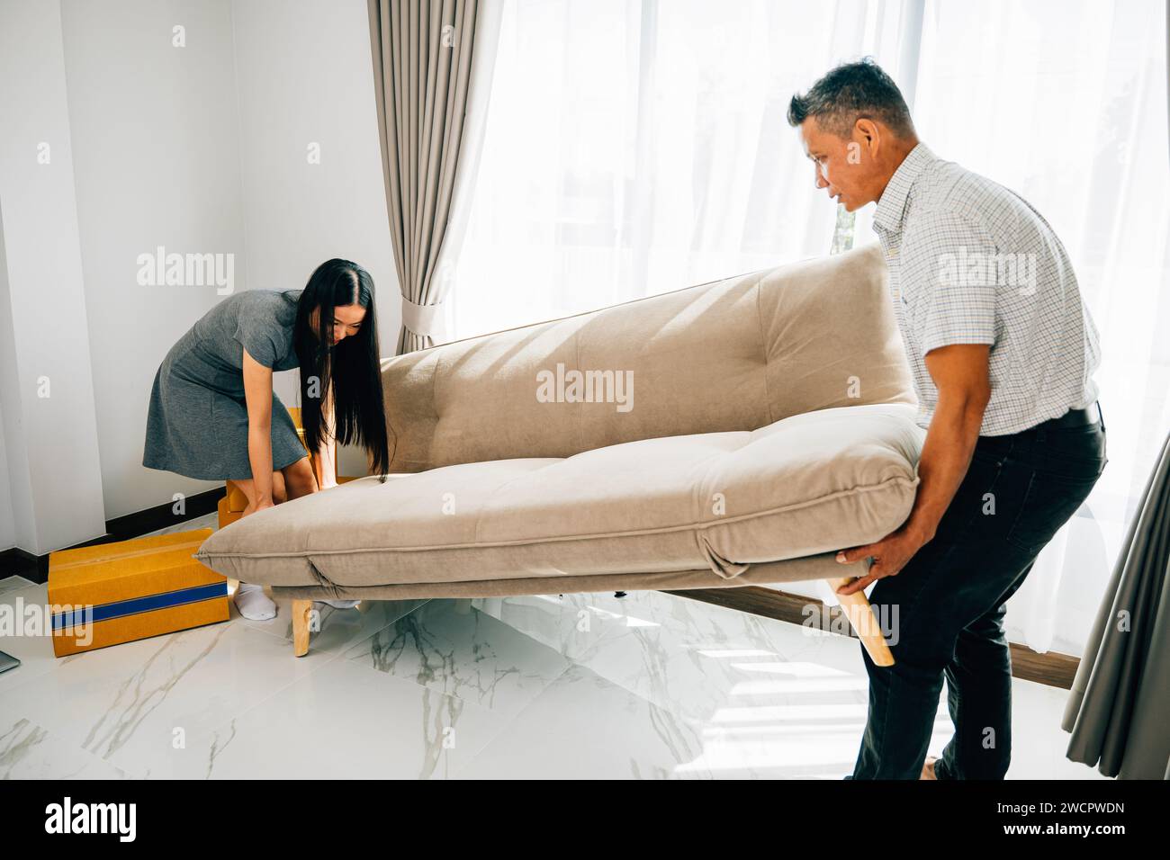 Asian couple smiles while moving a sofa in their new apartment Stock ...