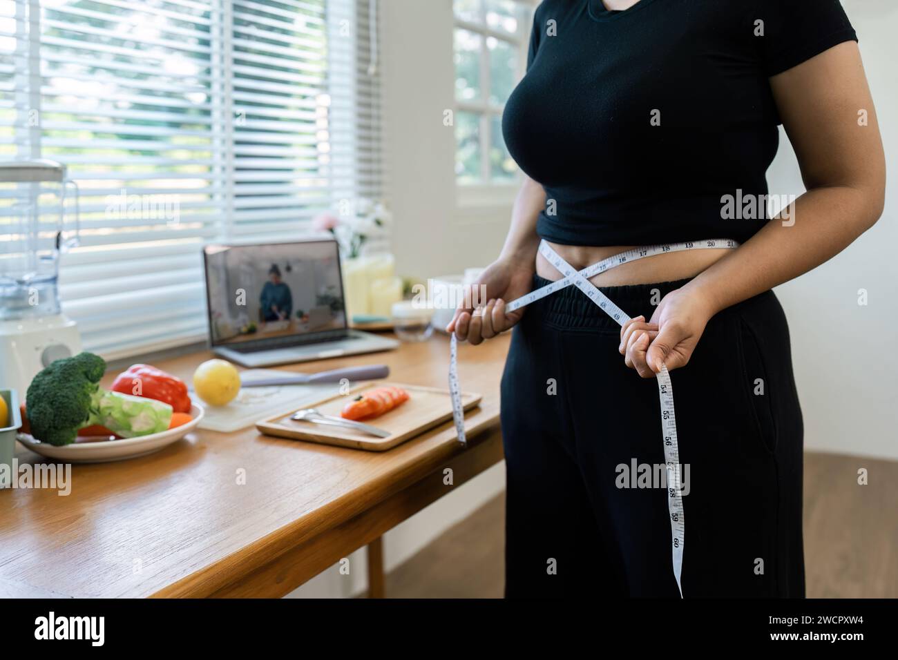 overweight Asian woman measuring her hip while learning to make salad ...