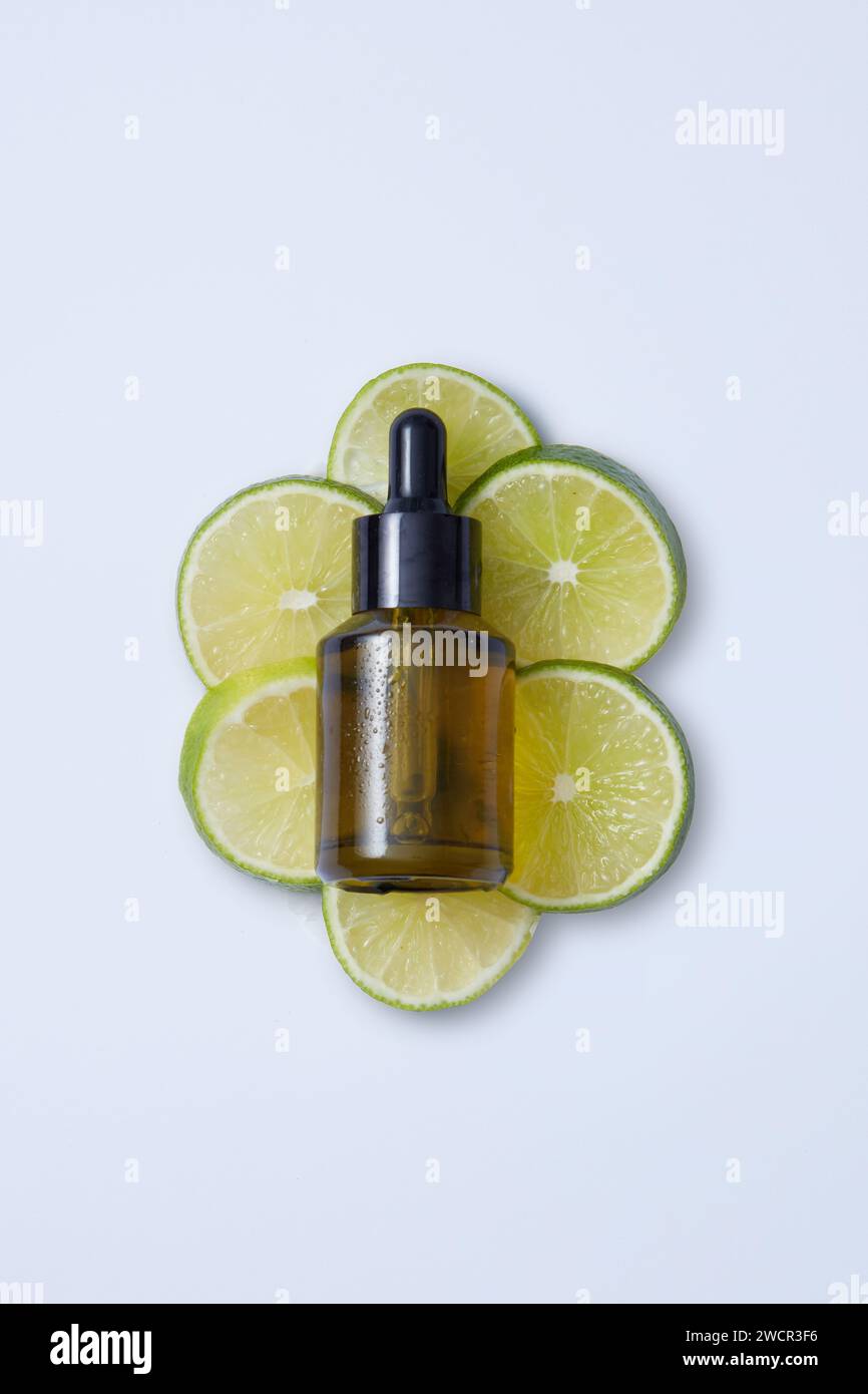 Unlabeled transparent bottle with dropper is placed on several lime ...