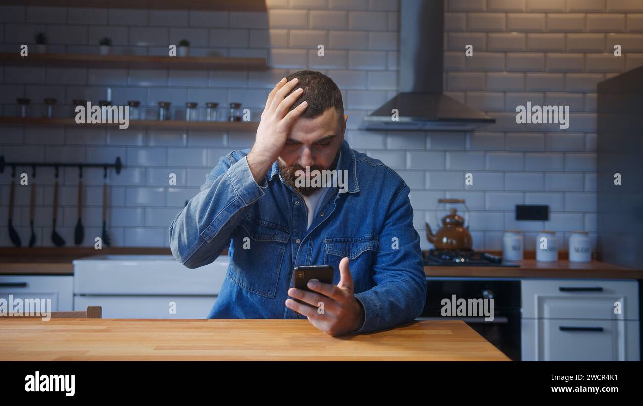 Young adult man sitting against the kitchen counter using smartphone ...