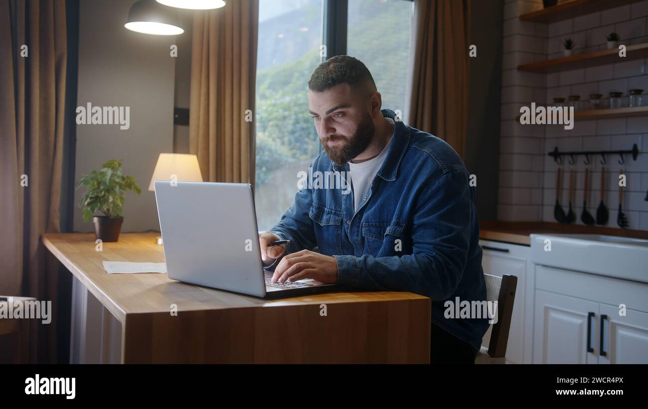 Bearded young adult business man sitting against the kitchen counter ...