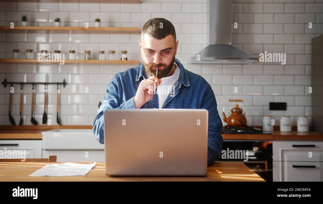Bearded young adult man typing on laptop doing research sitting against ...