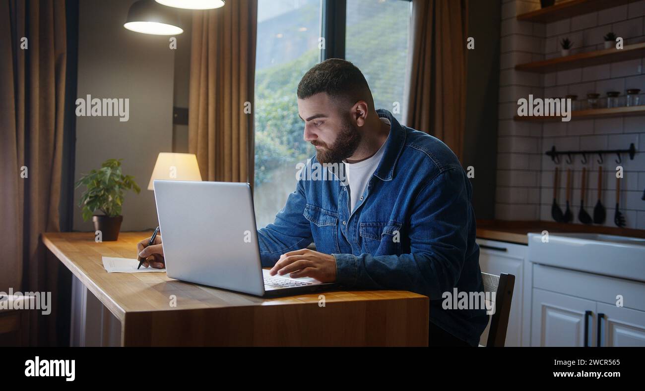 Bearded young adult business man sitting against the kitchen counter ...