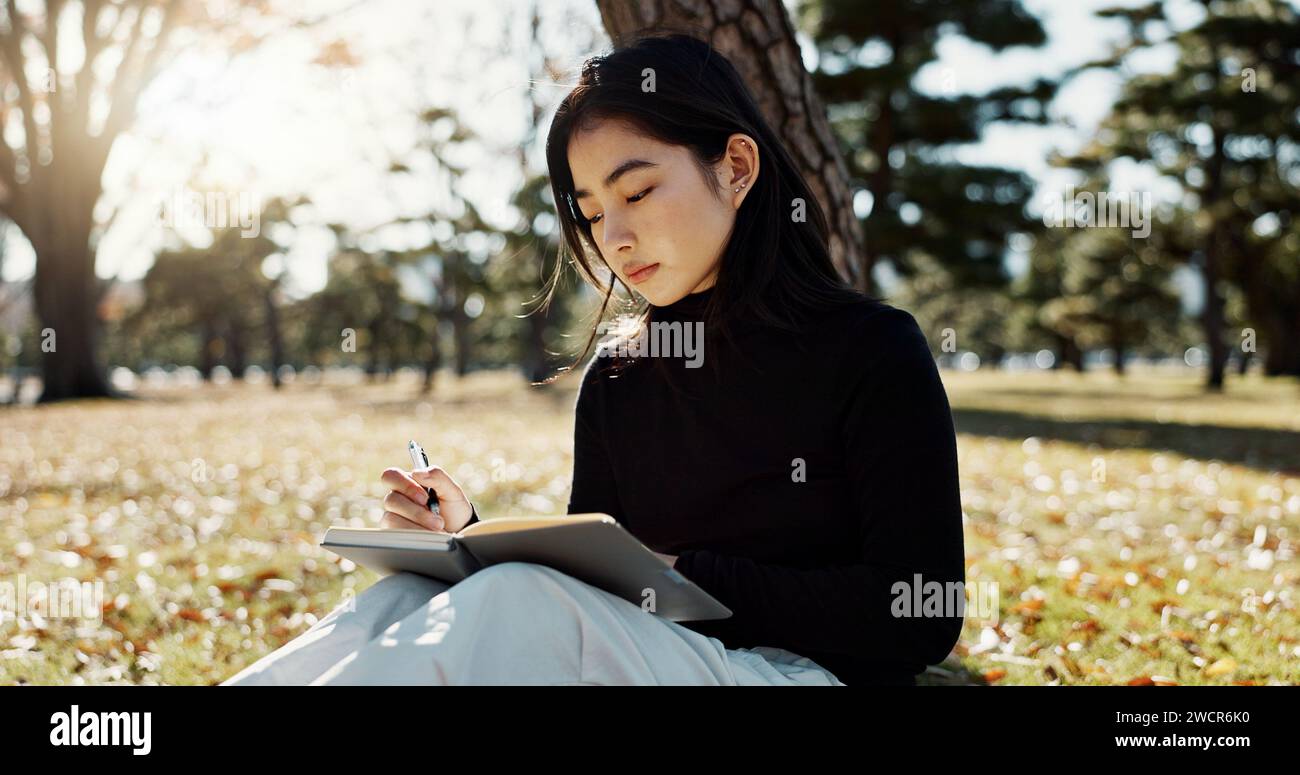 Japanese woman, writing and book in park, thinking and relax by tree ...