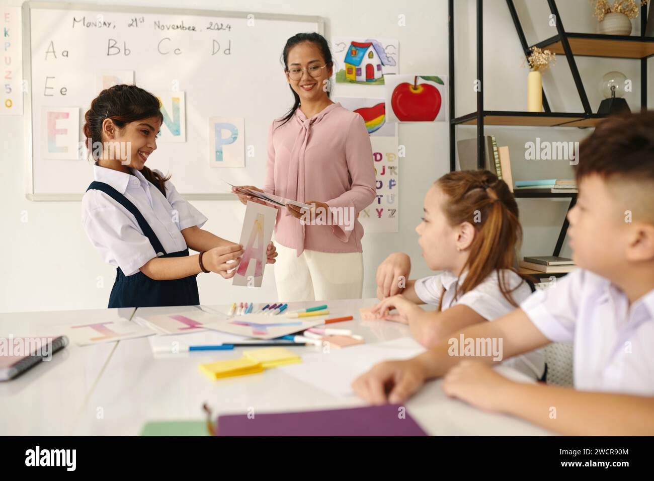 Smiling girl showing card with letter her classmates Stock Photo - Alamy