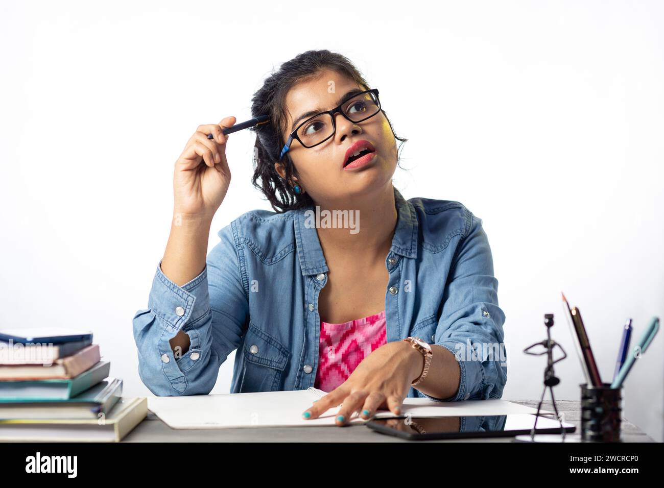 A pretty young Indian college student in eyeglasses thinking while ...