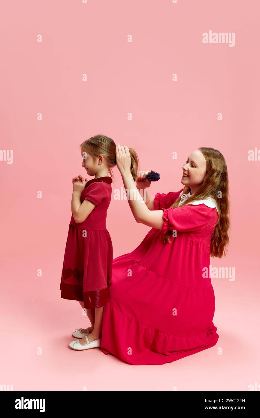 Girly moments. Beautiful young mother brushing daughter's hair, doing ...