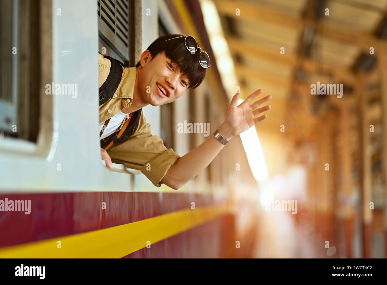 Happy young Asian man waving hand to friend through train window before ...