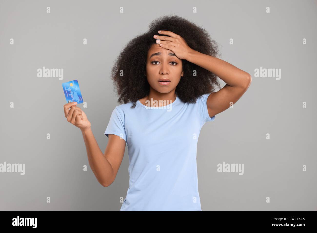 Confused woman with credit card on grey background. Debt problem Stock ...