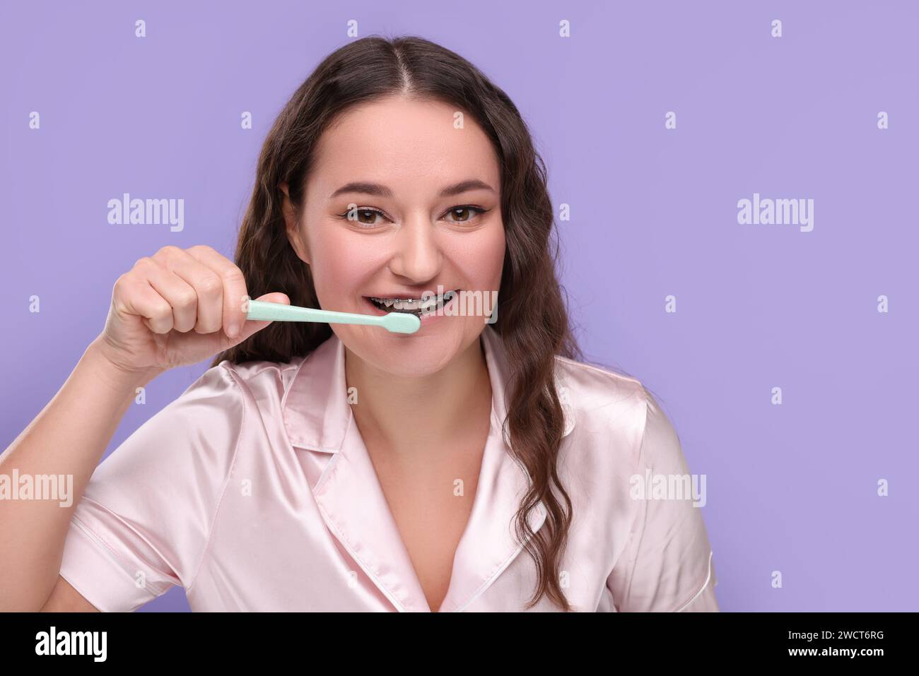 Woman with braces cleaning teeth on violet background. Space for text ...