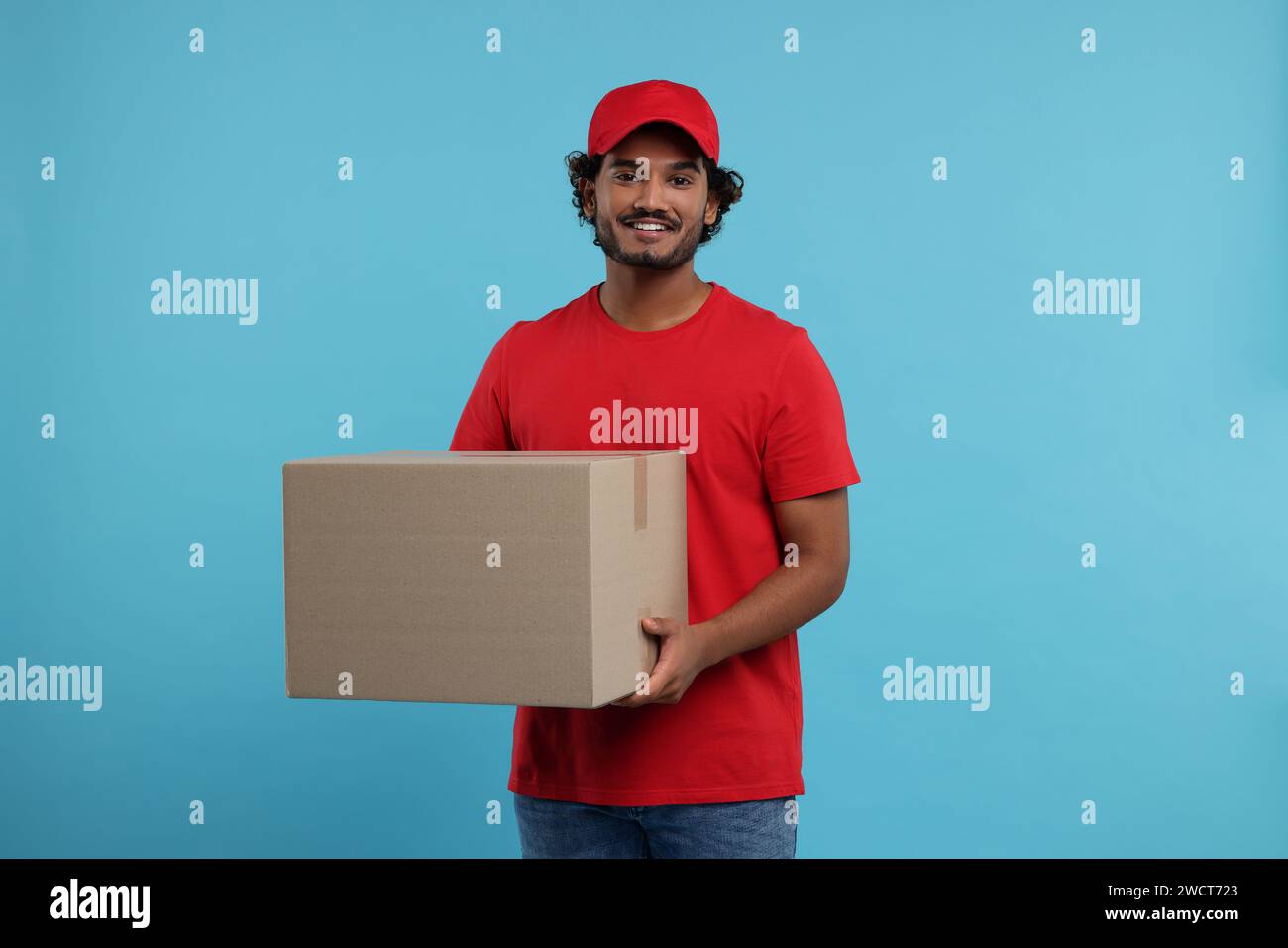 Happy young courier with parcel on light blue background Stock Photo ...