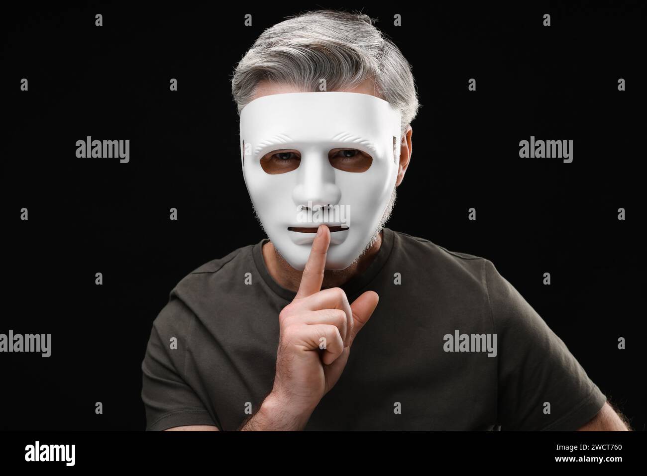 Man in mask showing hush gesture against black background Stock Photo ...