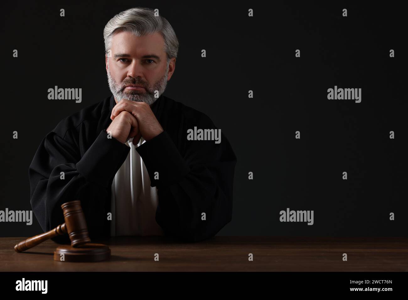 Judge with gavel sitting at wooden table against black background ...
