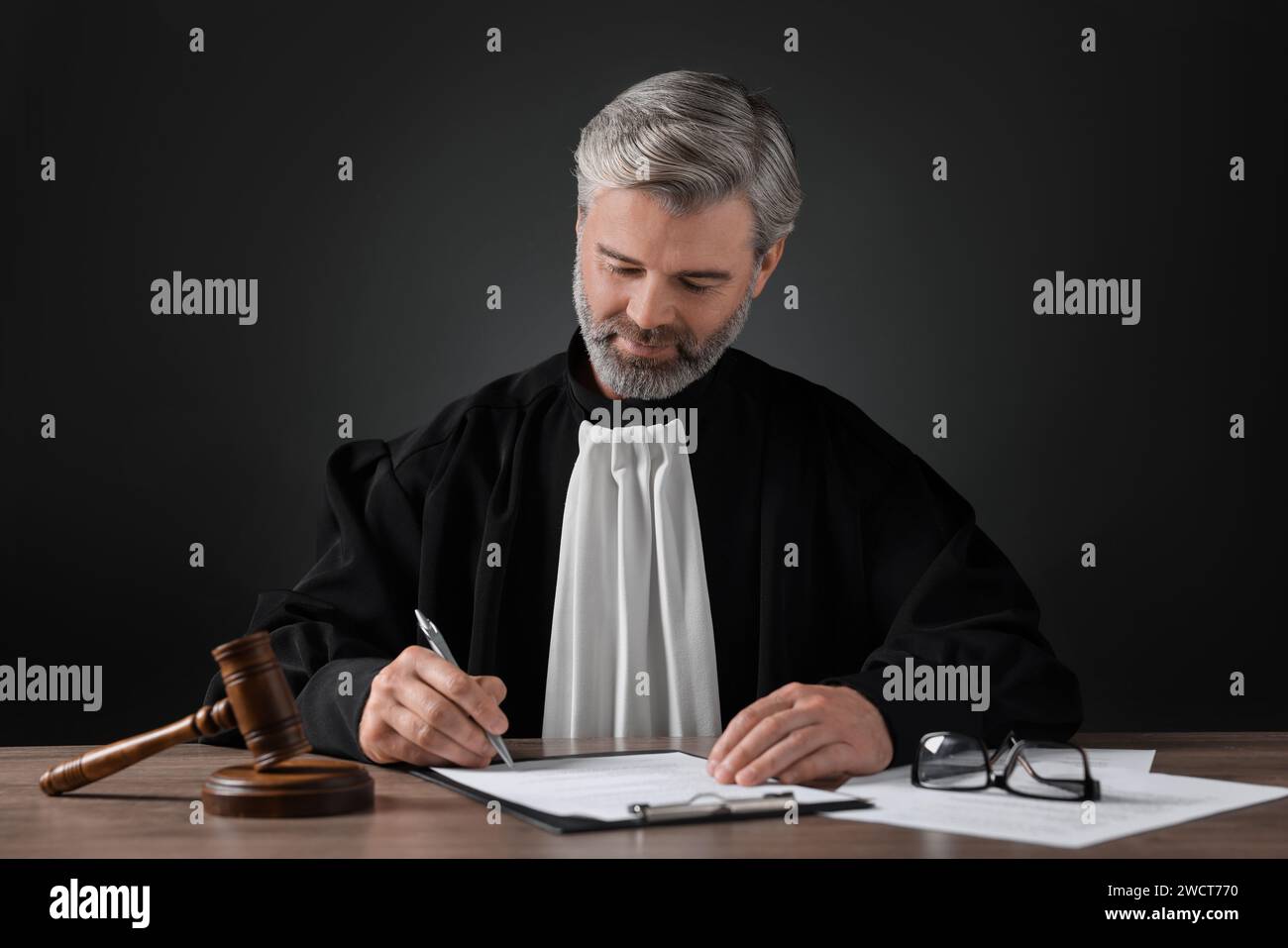 Judge working with documents at wooden table against black background ...