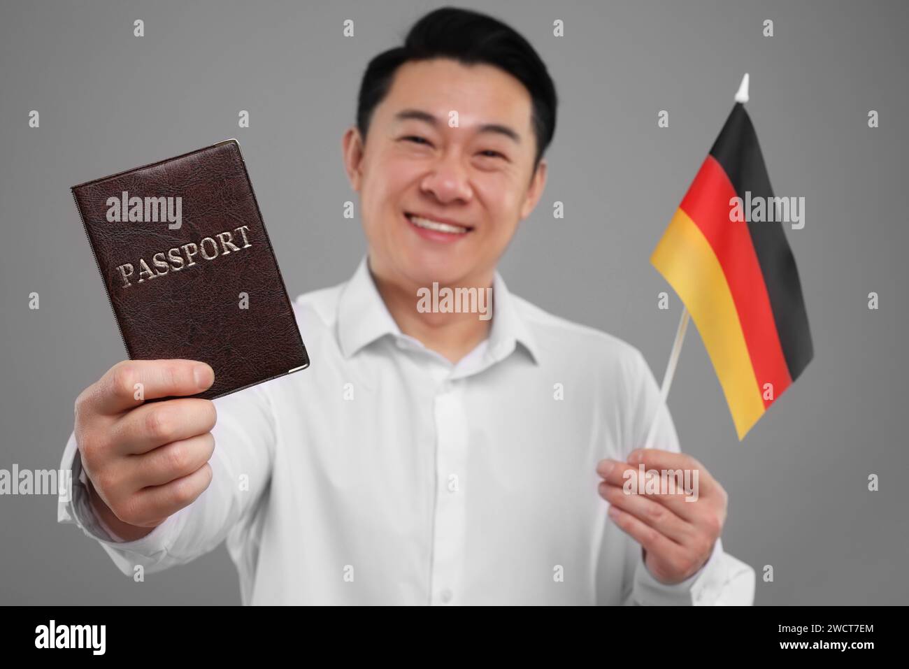 Immigration. Happy man with passport and flag of Germany on grey ...