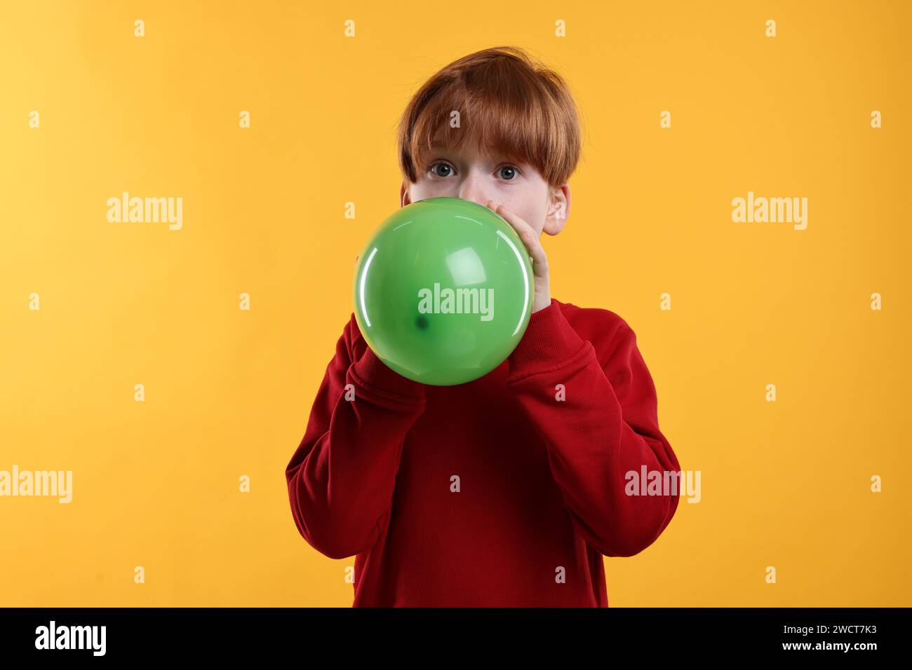 Boy inflating green balloon on orange background Stock Photo - Alamy