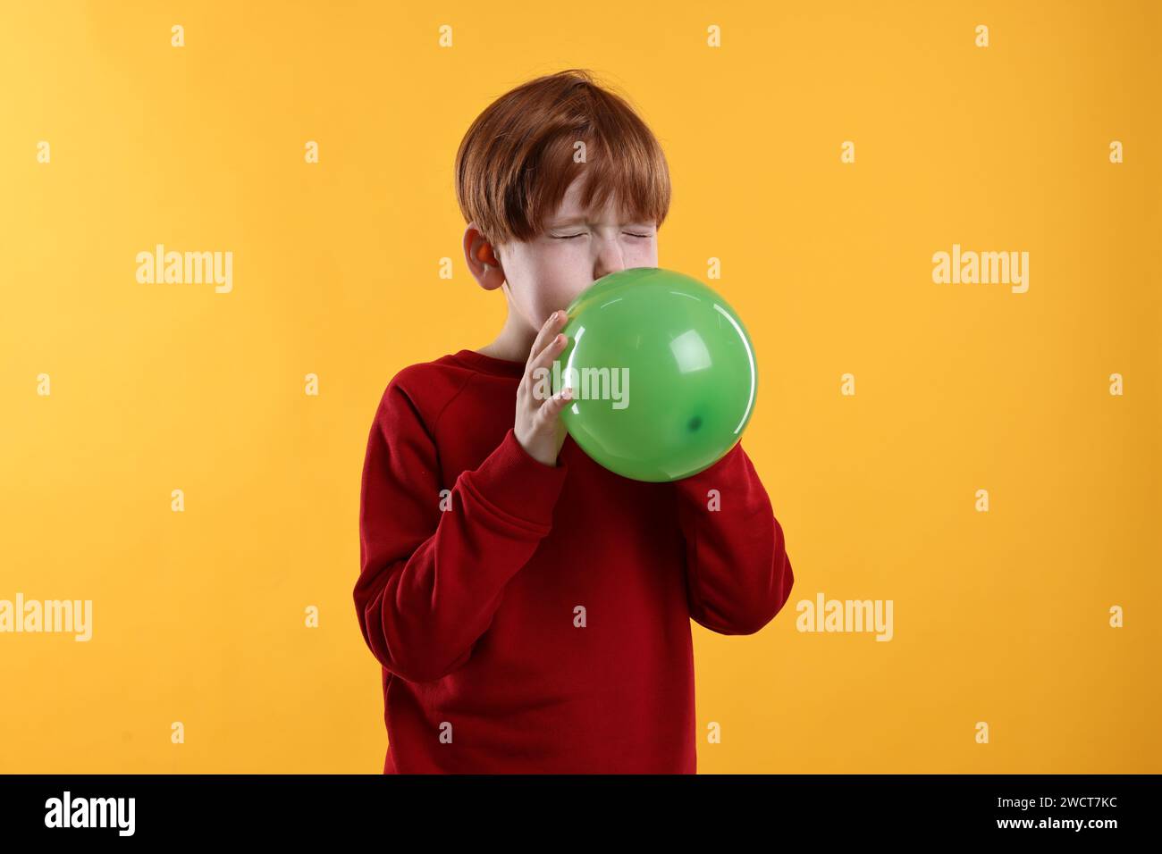 Boy inflating green balloon on orange background Stock Photo - Alamy