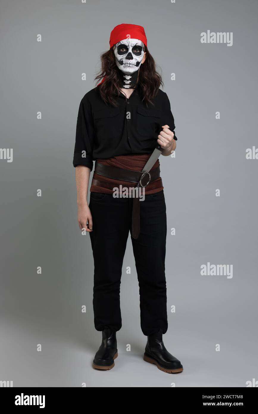Man in scary pirate costume with skull makeup and knife on light grey ...