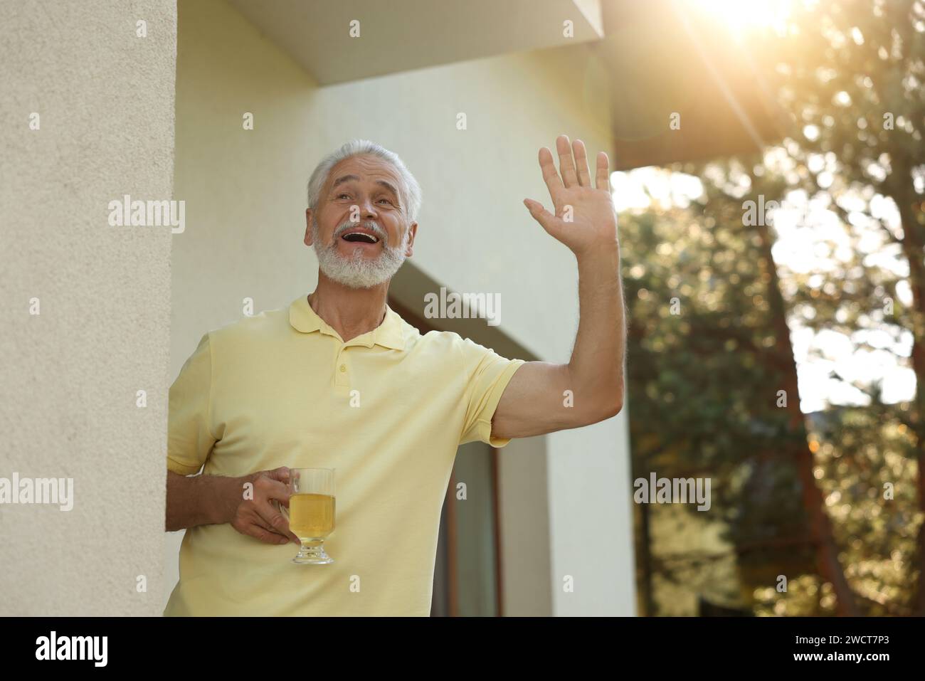 Neighbor greeting. Happy senior man with cup of tea waving near house ...