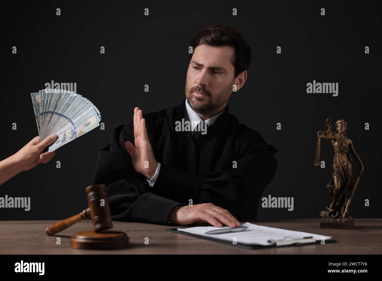 Woman giving bribe to judge at wooden table against black background ...